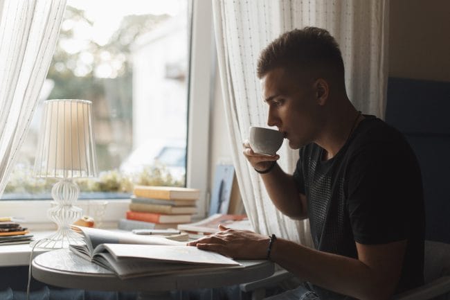 Young man rest in a restaurant, reading a book and drinking coff ...